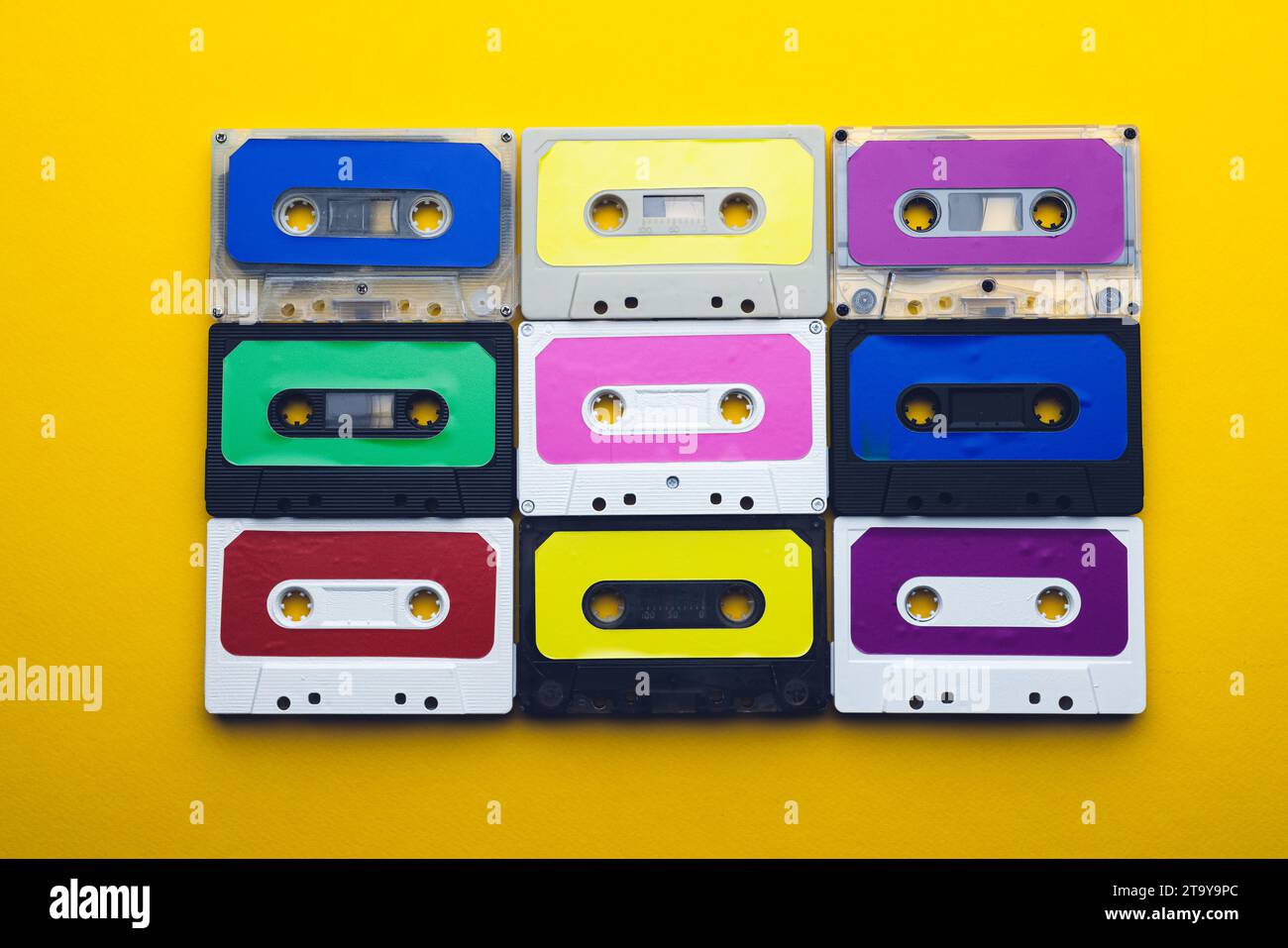 Overhead view of nine colourful cassette tapes arranged on yellow ...