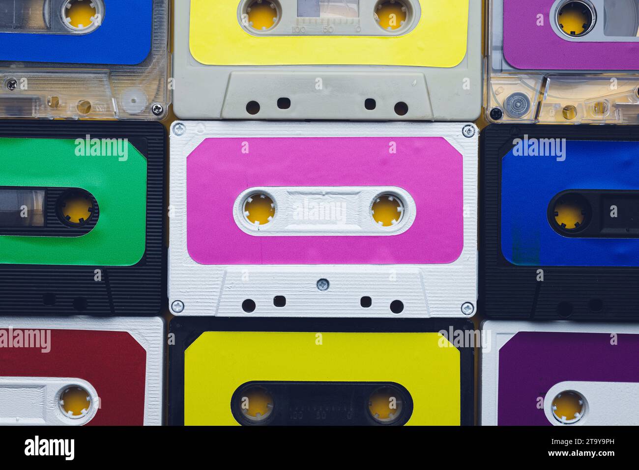Overhead view of nine colourful cassette tapes arranged on yellow ...