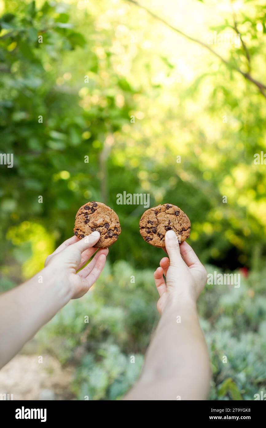 Vertical view of two kids friends holding and sharing cookies with park ...