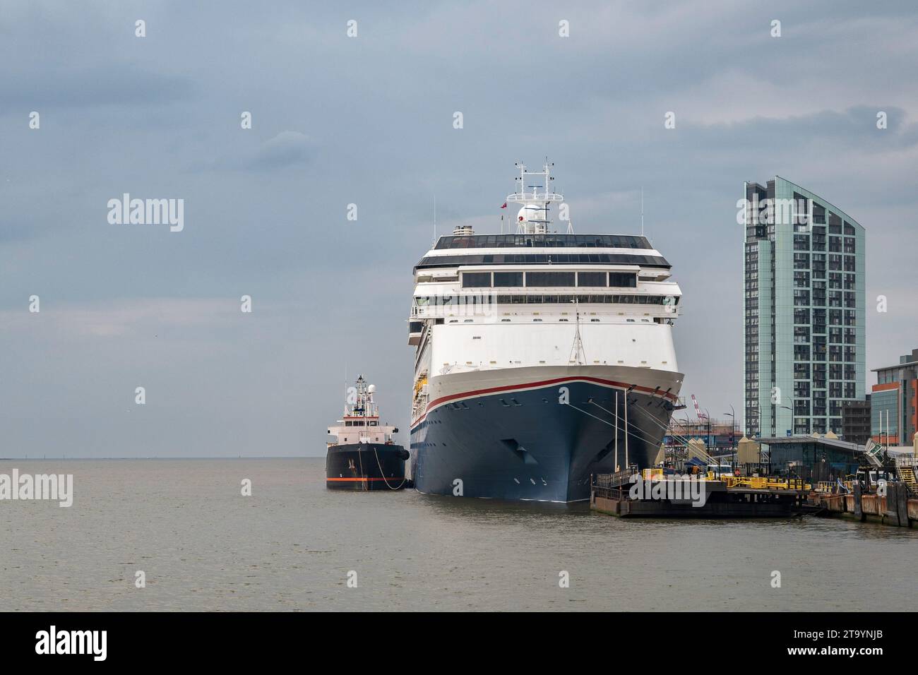 A huge cruise ship, docked in Liverpool, England, with a small tug boat ...