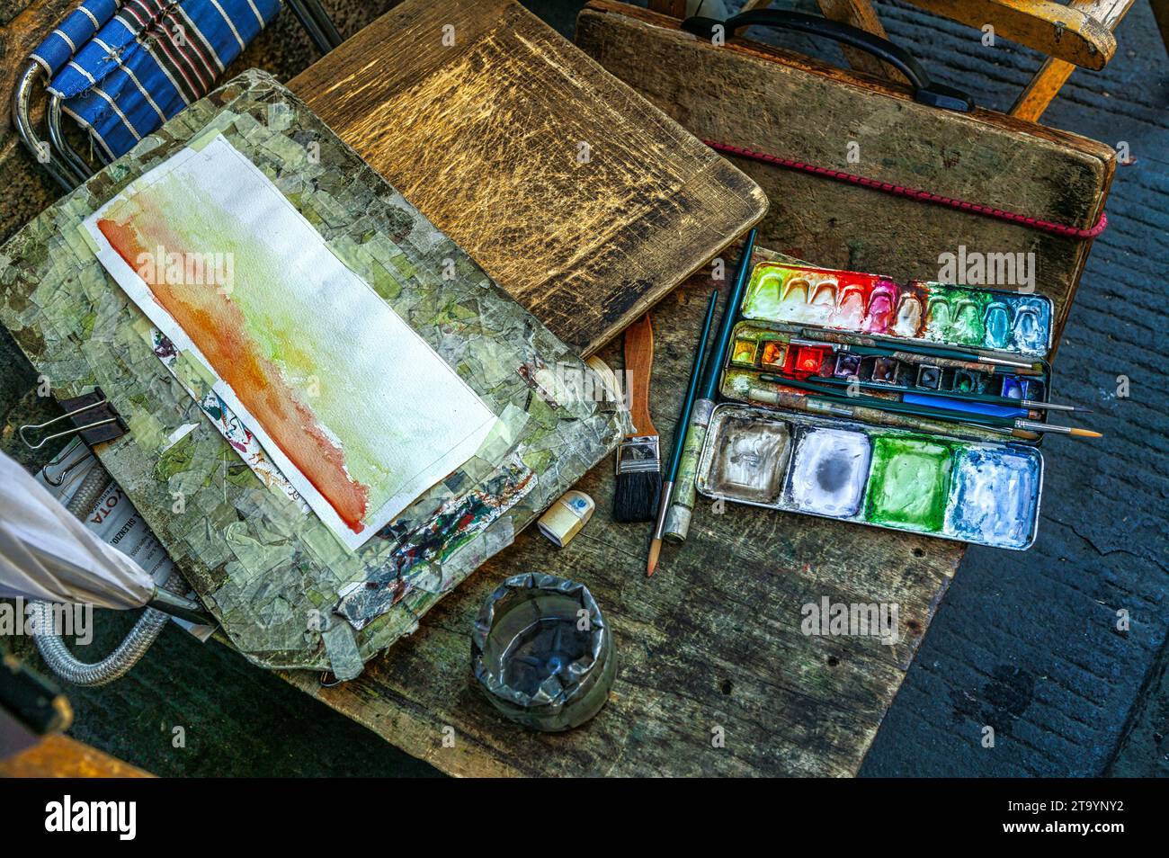 Work table of a street painter. Color palette, brushes and a watercolor ...