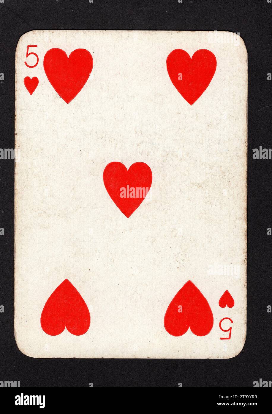 A vintage five of hearts playing card isolated on a black background ...