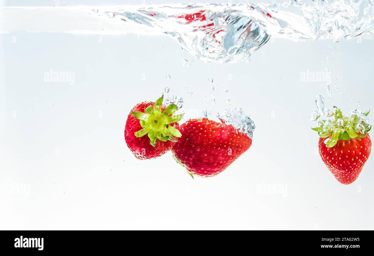 red fresh fruit strawberries falling into water with splash on white ...