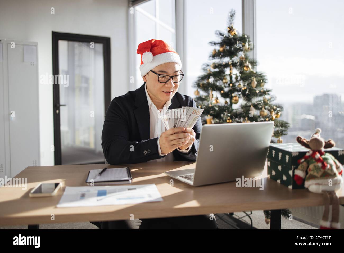 Adult asian rich business man in Santa hat working on laptop counting ...