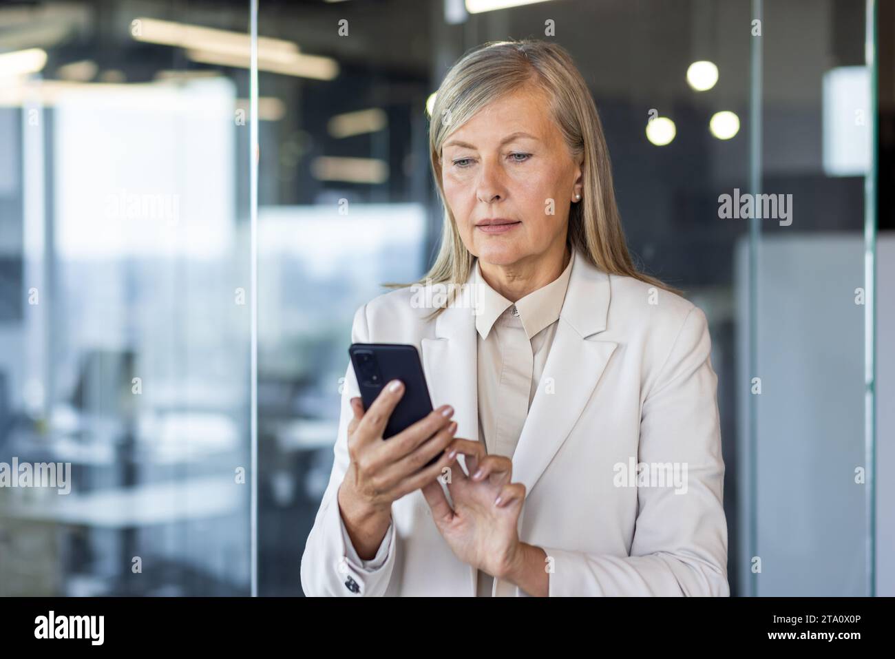 Serious gray-haired businesswoman standing in the office and using the ...