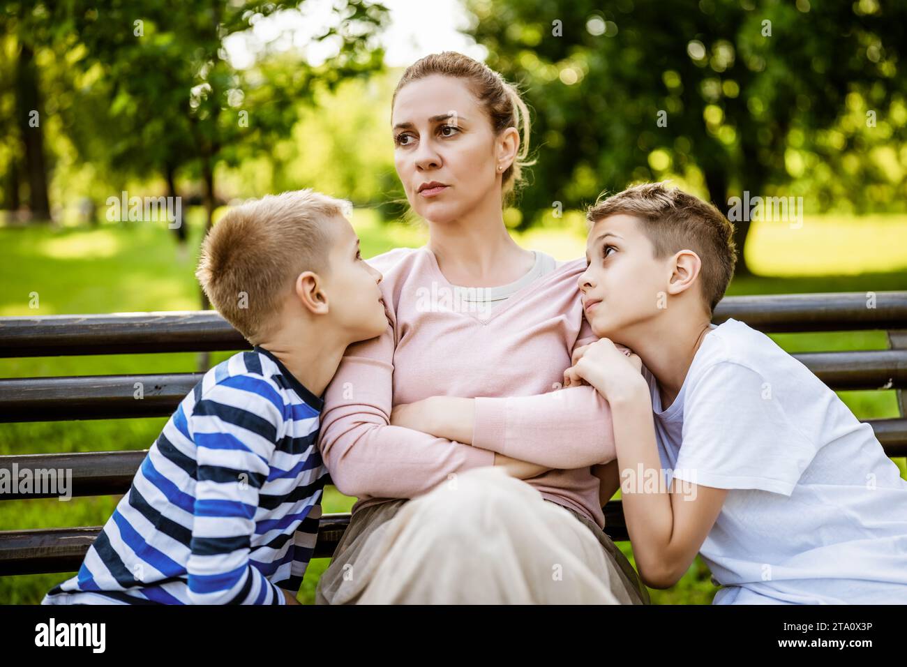 Mother is sitting with her sons on bench in park. She is angry and the ...