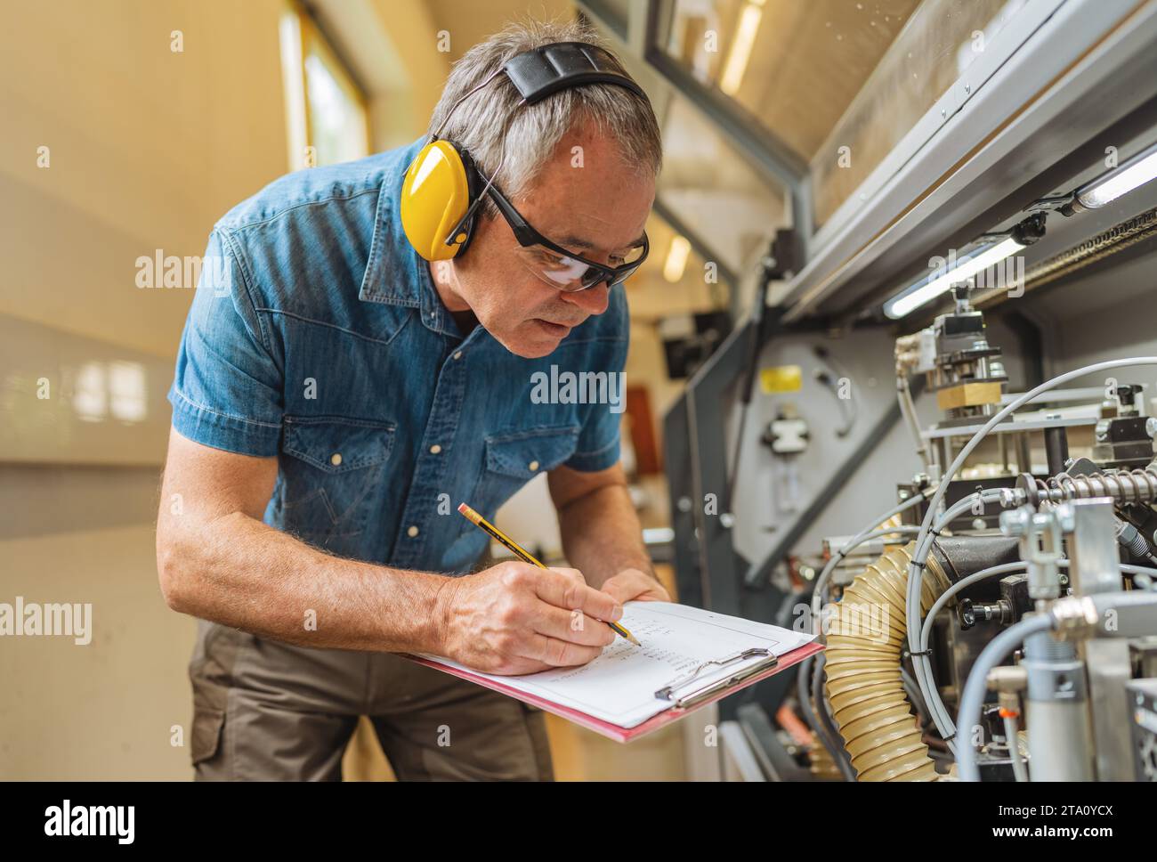 Technician with ear protection writing on clipboard in industrial ...
