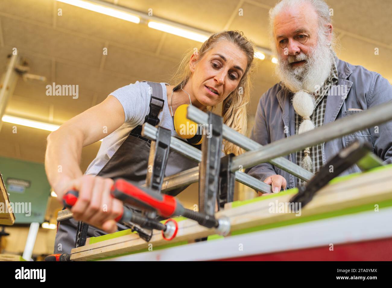 Master carpenter and apprentice using a clamp for wood gluing in a ...