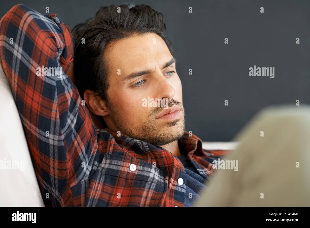 Thinking, mistake or shame with a man on a sofa in the living room of ...