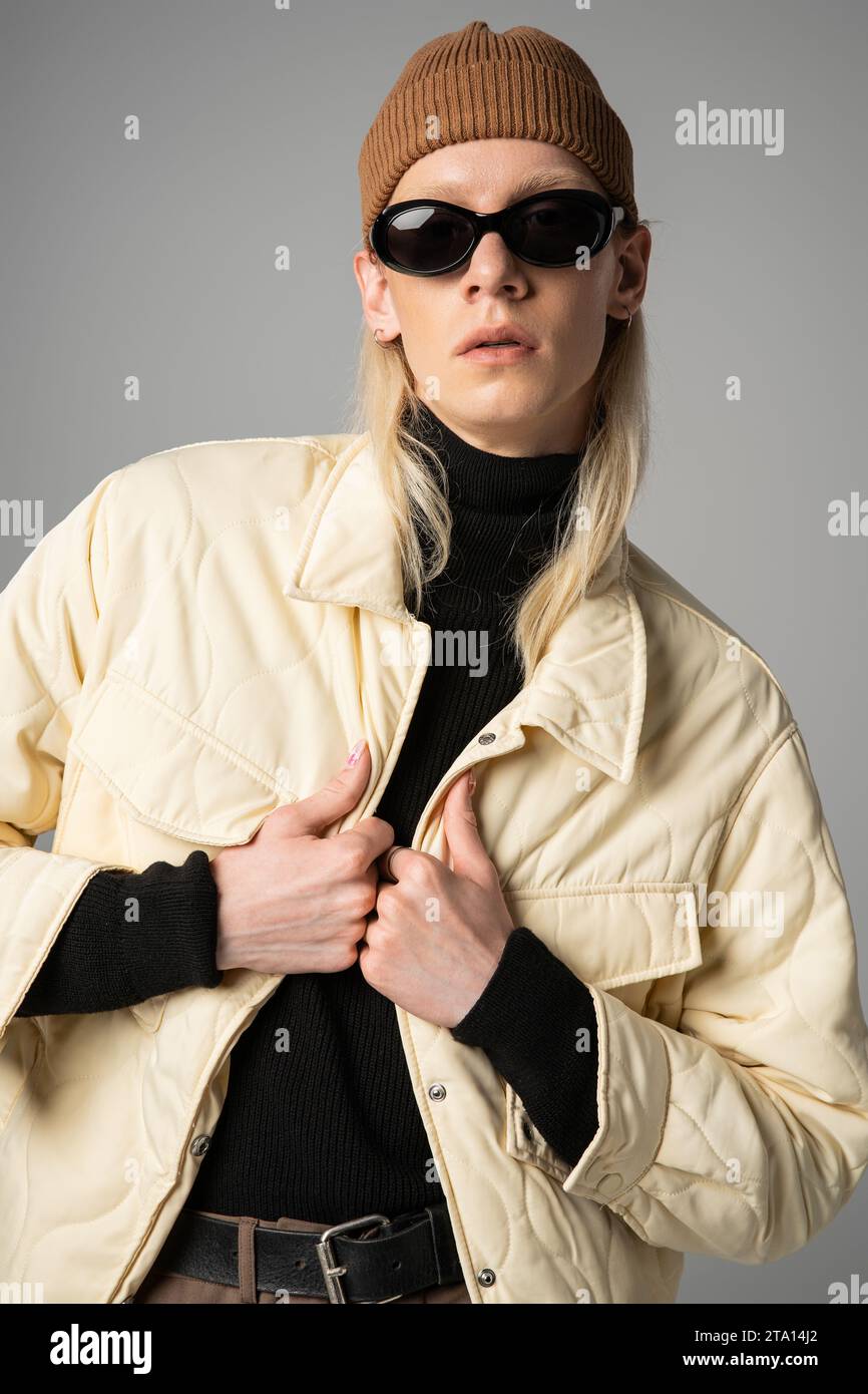 attractive non binary person in stylish winter attire posing on gray ...