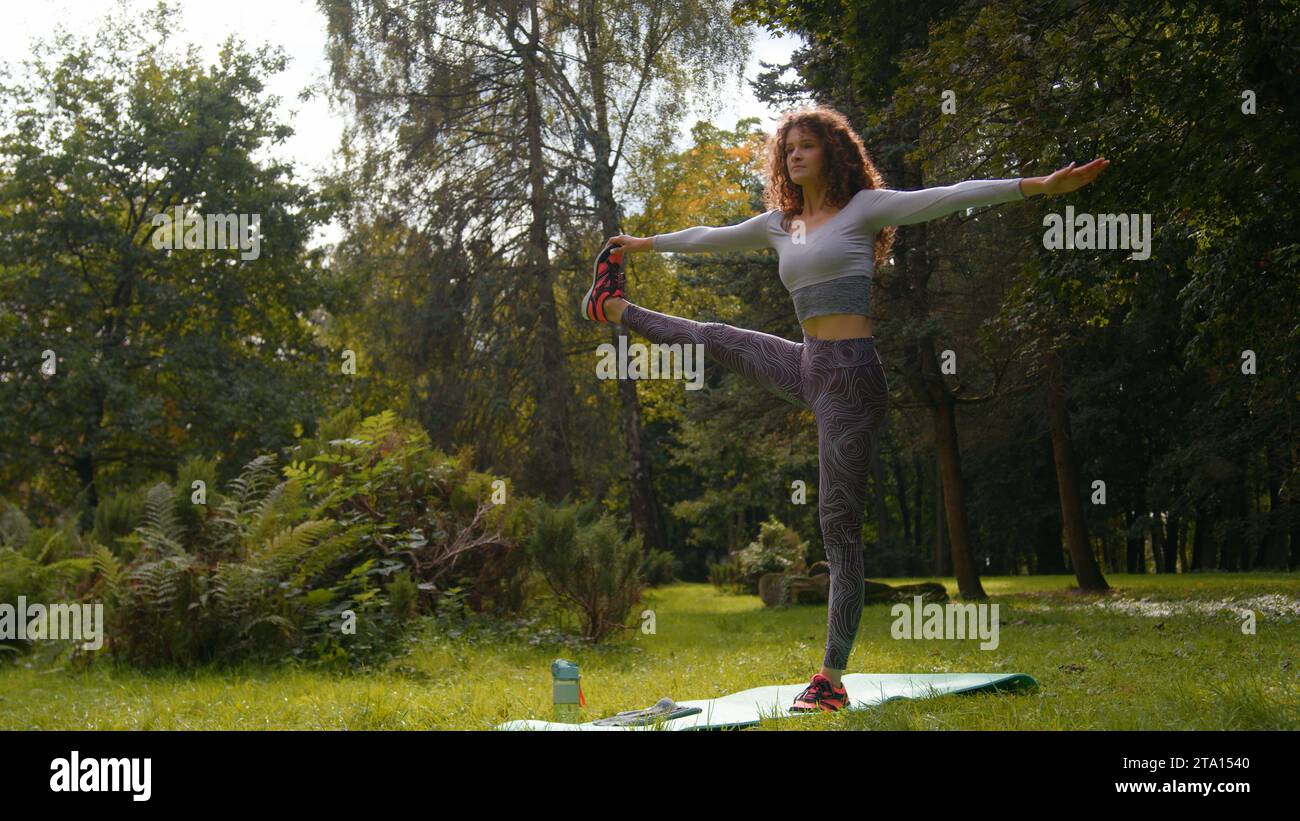 Caucasian flexible strong girl woman lady standing park nature summer outdoors doing yoga ...