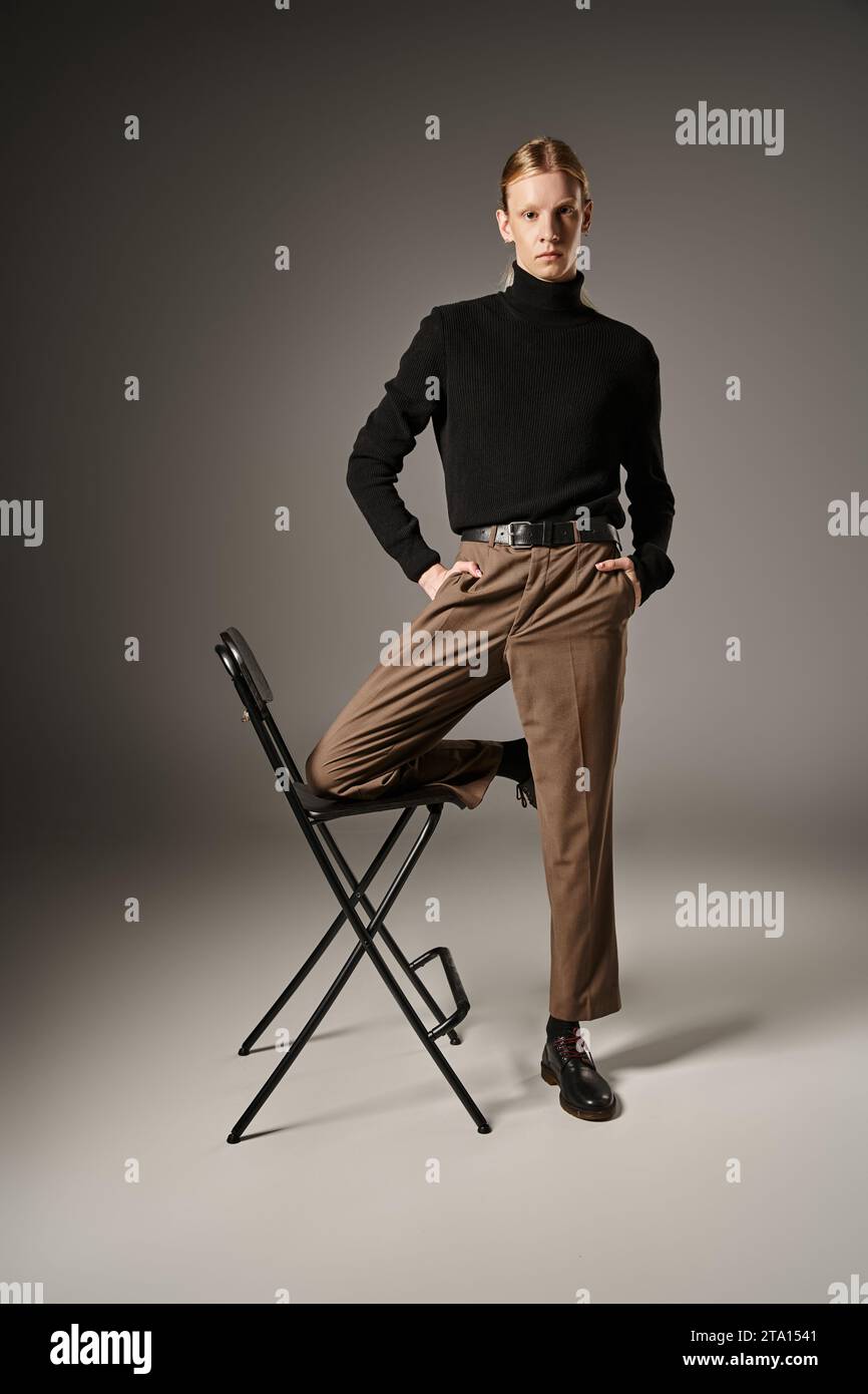 attractive non binary model with ponytail posing with knee on black ...