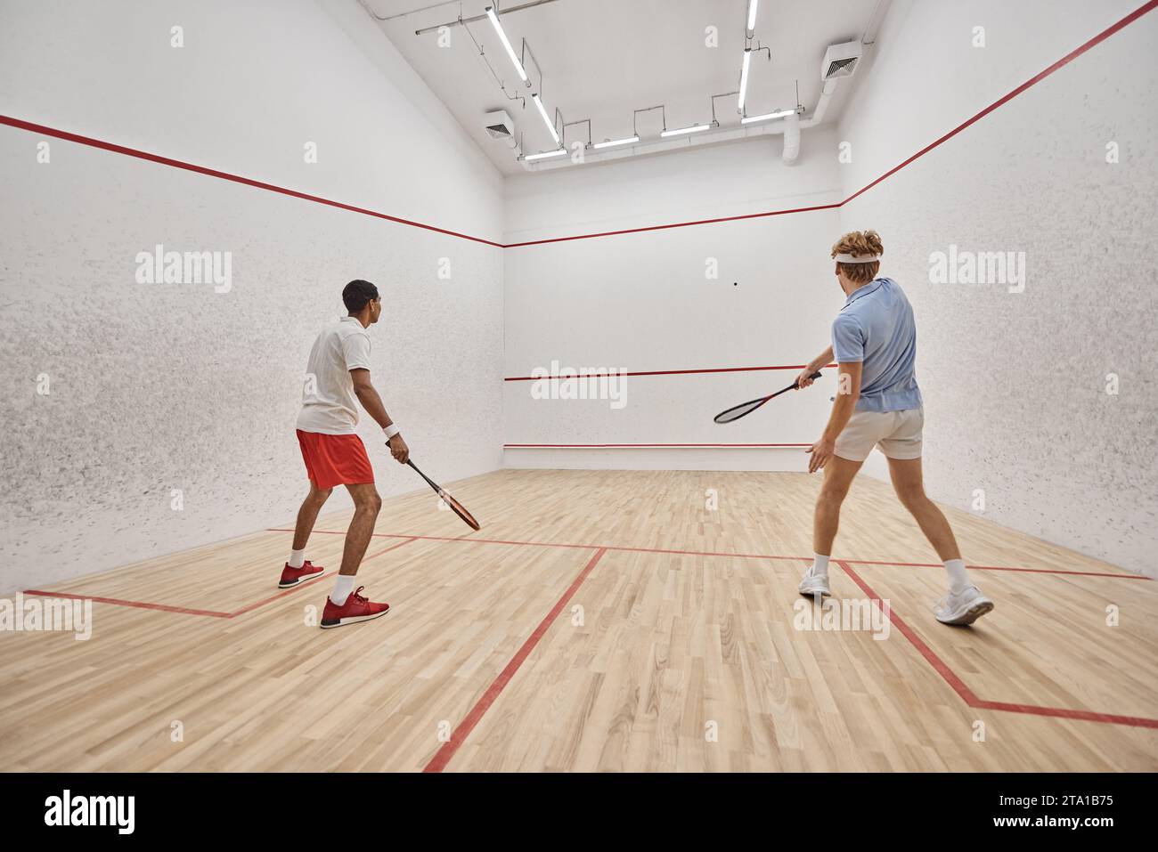 dynamic and interracial friends playing squash together inside of court ...