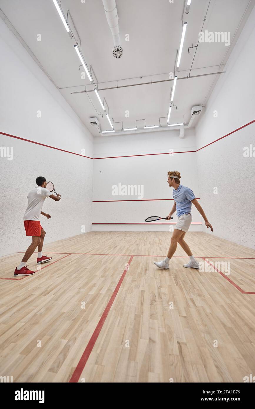 dynamic interracial sportsmen playing squash together inside of court ...