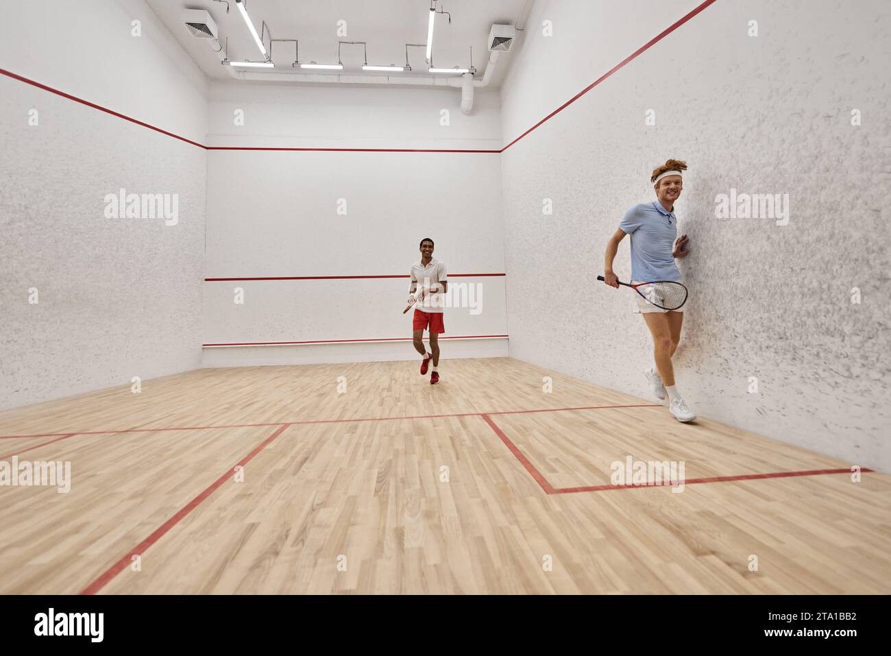 dynamic interracial players playing squash together inside of court ...