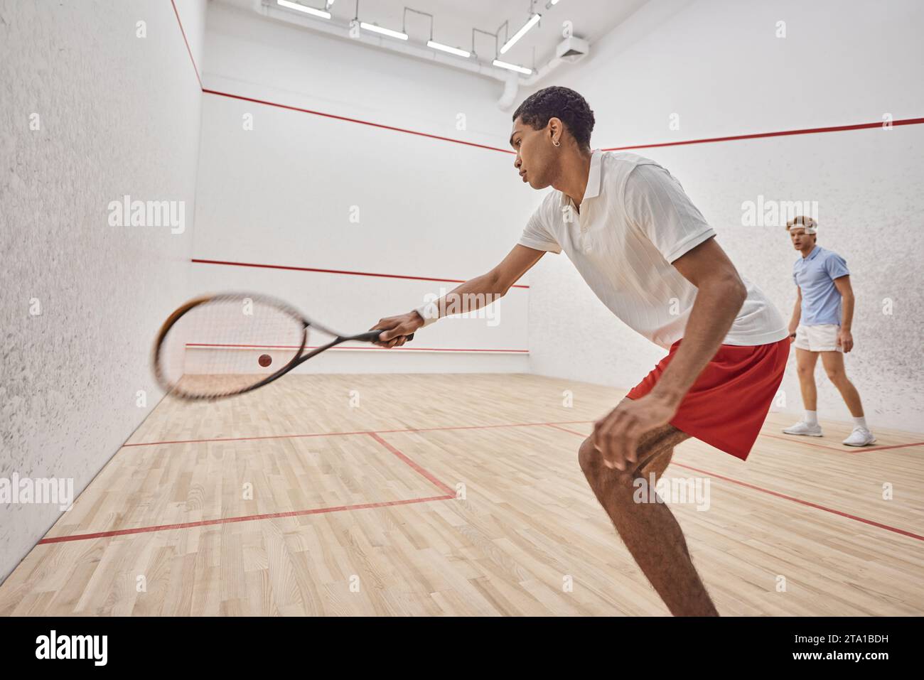 young and active multicultural men playing squash inside of court ...