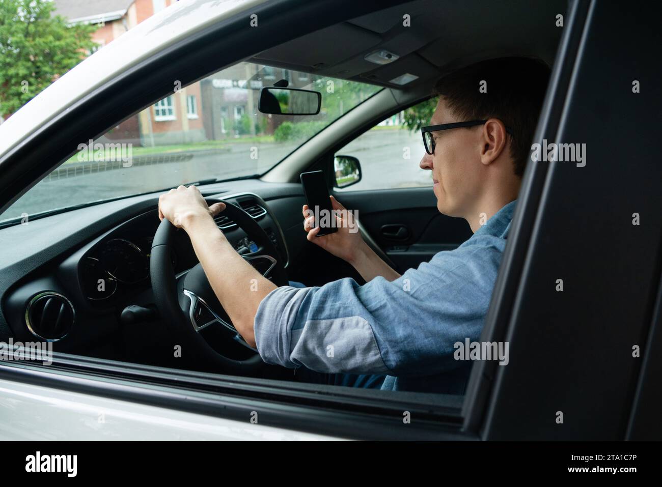 Male driver sits in a car and looks at a smartphone screen Stock Photo ...