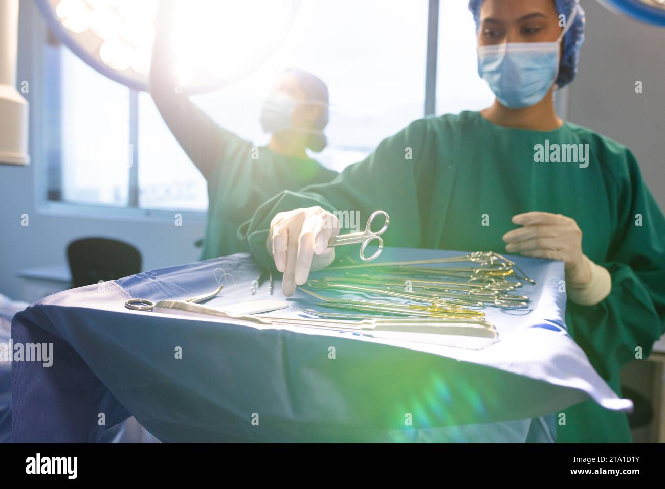 Biracial female surgeon with face mask taking surgical tool in hospital ...