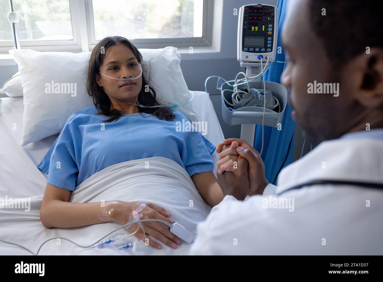 Diverse male doctor holding hand of female patient with iv drip in bed ...