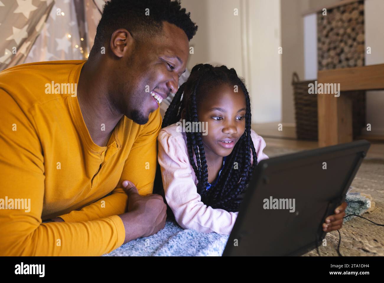 Happy african american father and daughter lying by teepee with ...