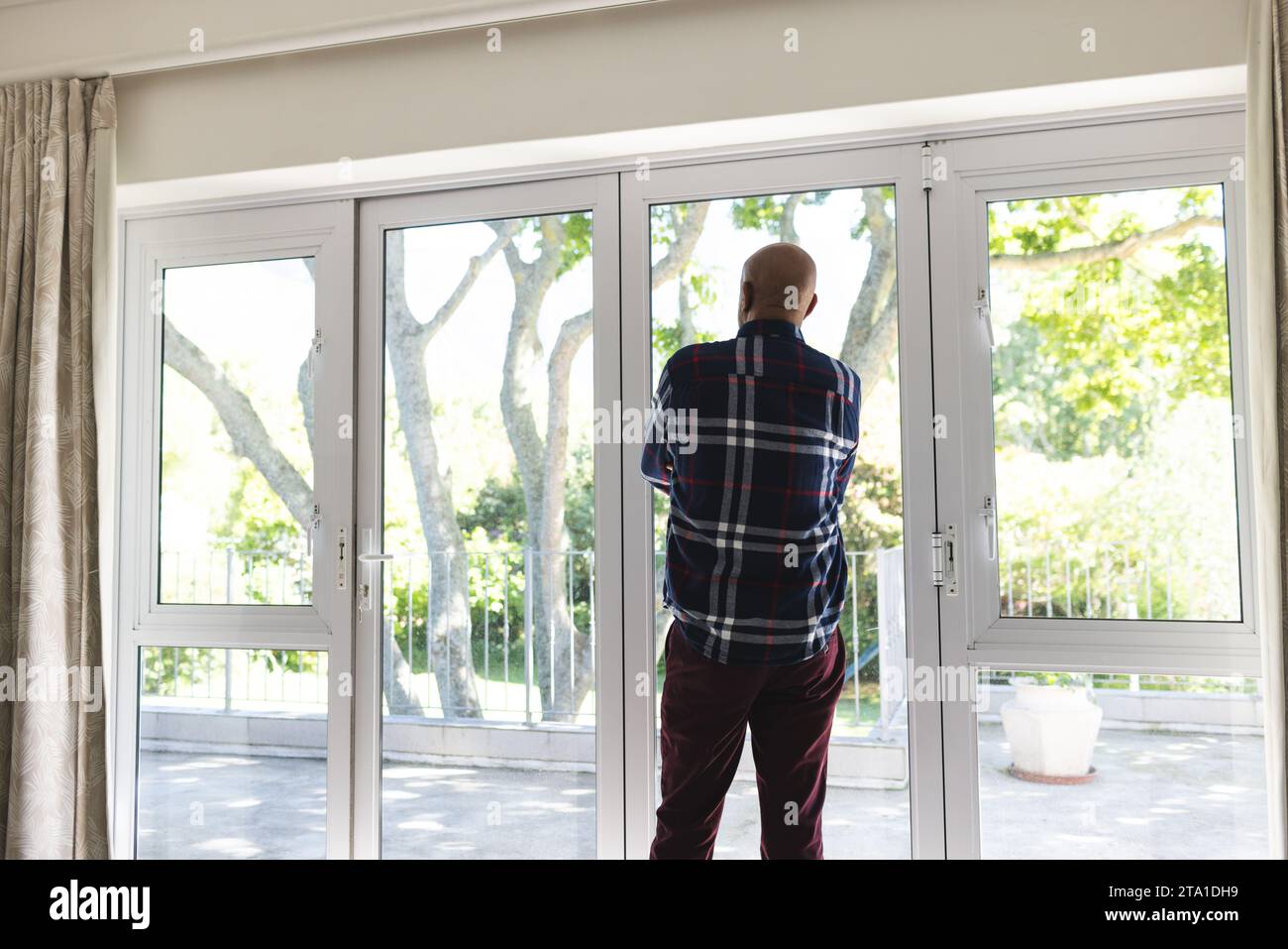 Back of african american senior man looking out window at home with ...