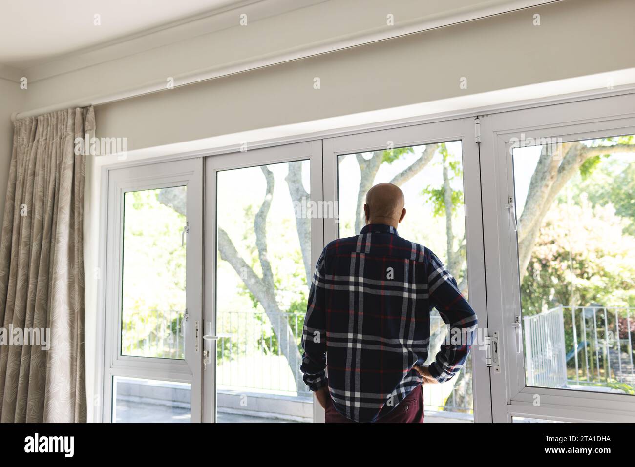 Back of african american senior man looking out window at home with ...