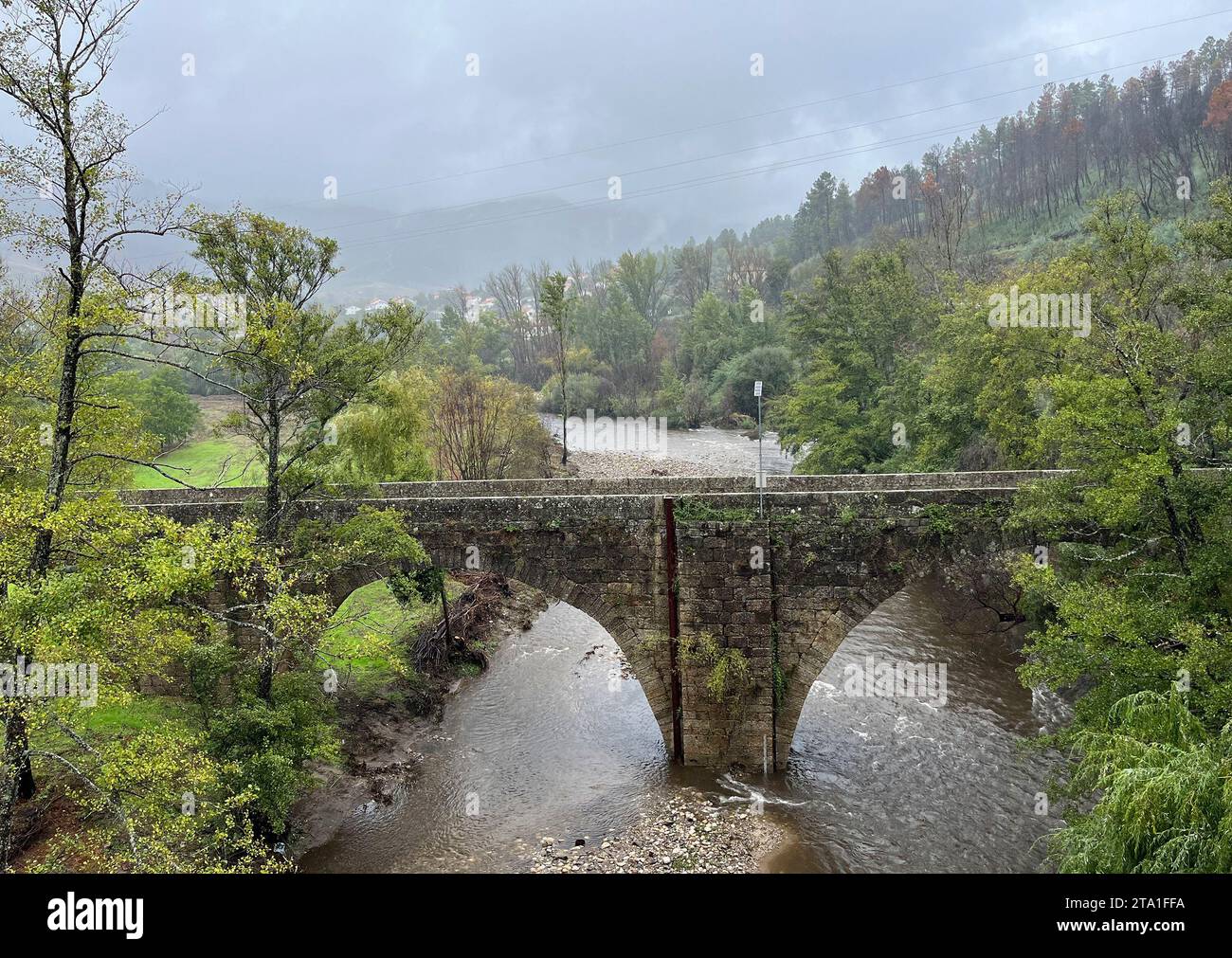 An old stone bridge crosses the Zêzere River in the Parque Nacional da ...