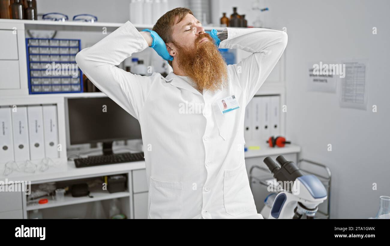 Exhausted young redhead man scientist stretching back in busy lab ...