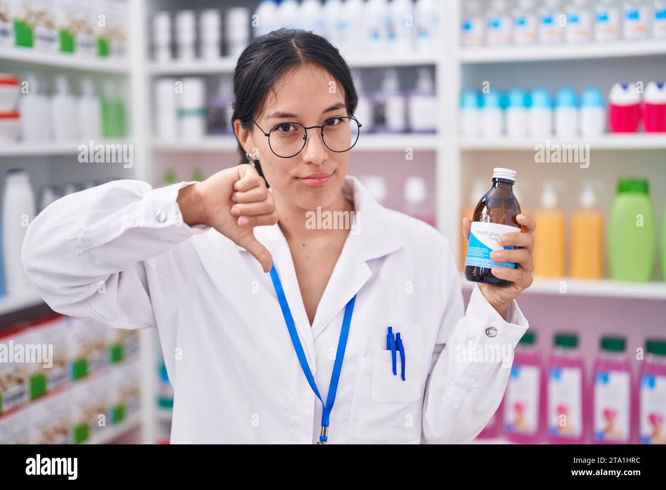 Young hispanic woman working at pharmacy drugstore holding syrup with ...