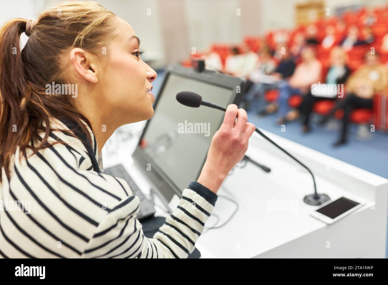 Female speaker giving speech through microphone at stage in seminar at ...