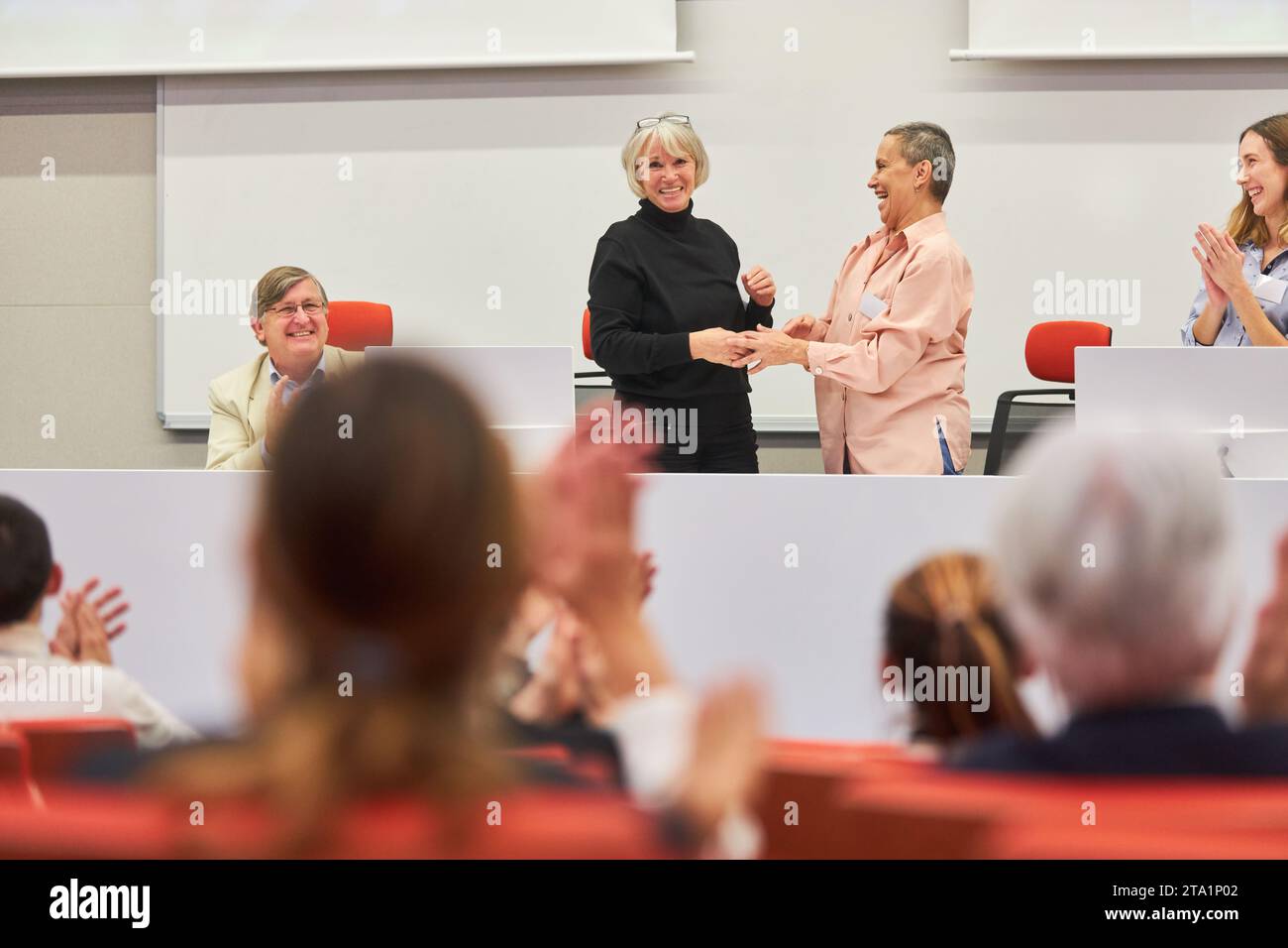 Female orators handshaking on stage in front of audience at business ...