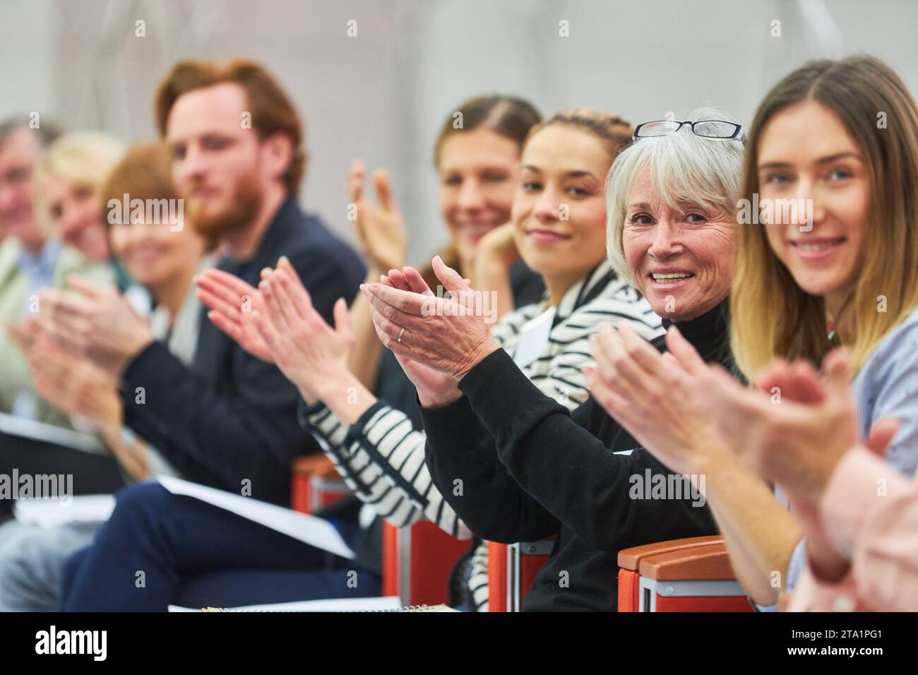 Portrait of smiling professionals clapping while sitting in audience at ...