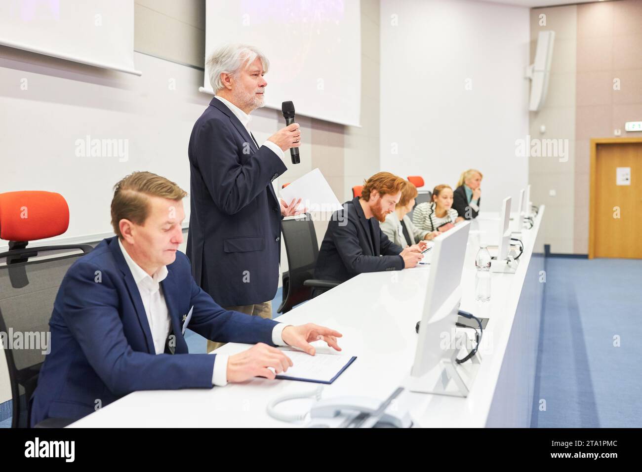 Male speaker explaining while standing by professionals on stage in ...