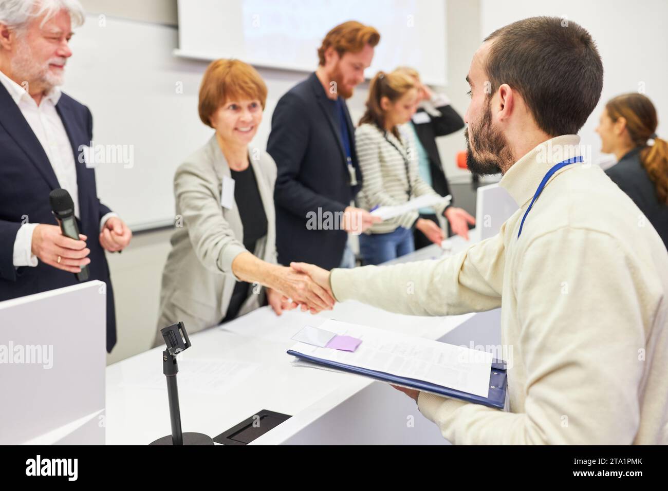 Female orator handshaking with man at panel during business event in ...