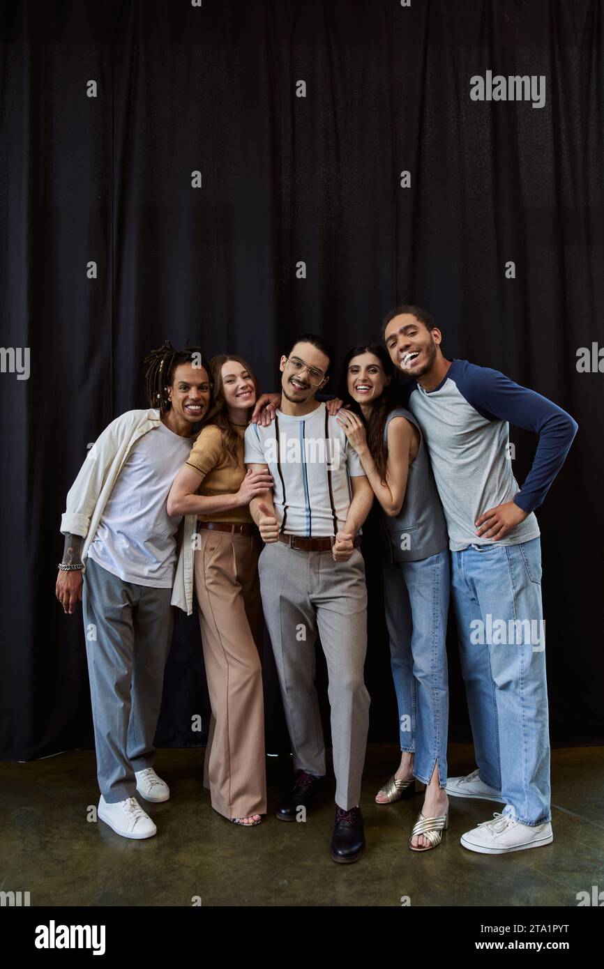 full length of happy and stylish multicultural team posing on black ...