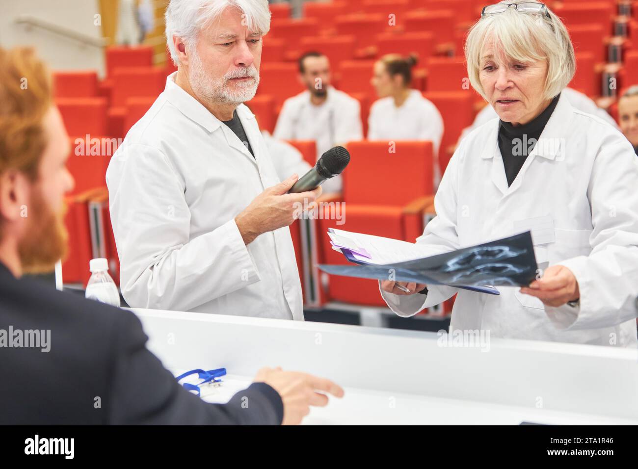 Male and female doctors discussing over x-ray in front of speaker ...