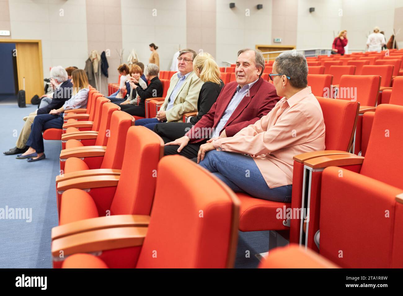 Male and female professionals talking while sitting in red chairs at ...