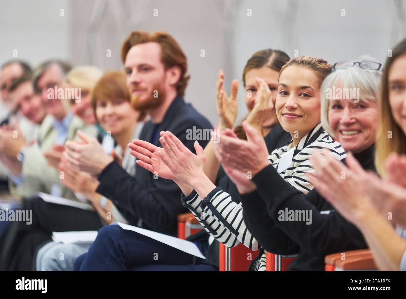 Portrait of smiling professionals clapping while sitting in audience at ...