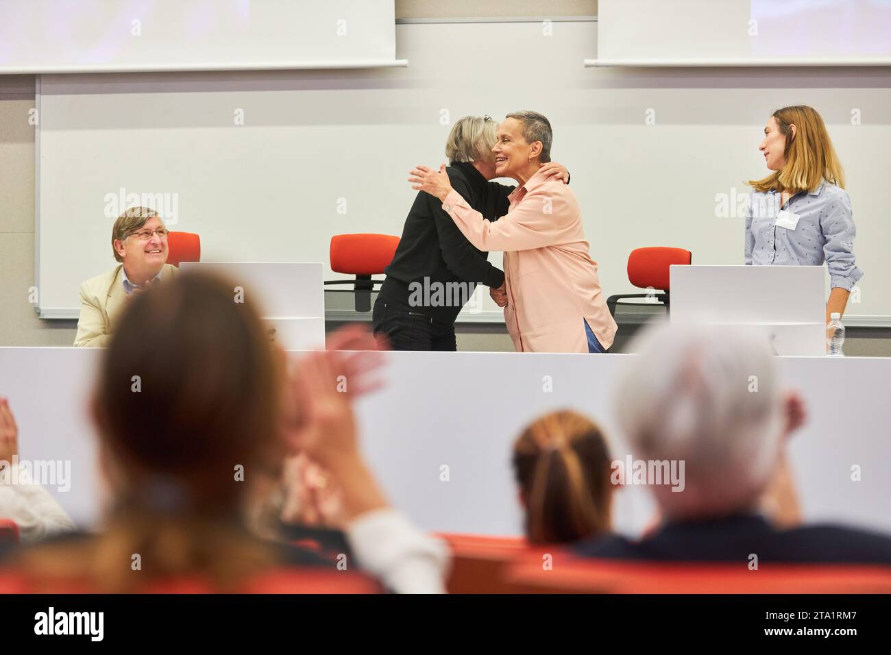 Female professionals embracing on stage in front of audience at ...