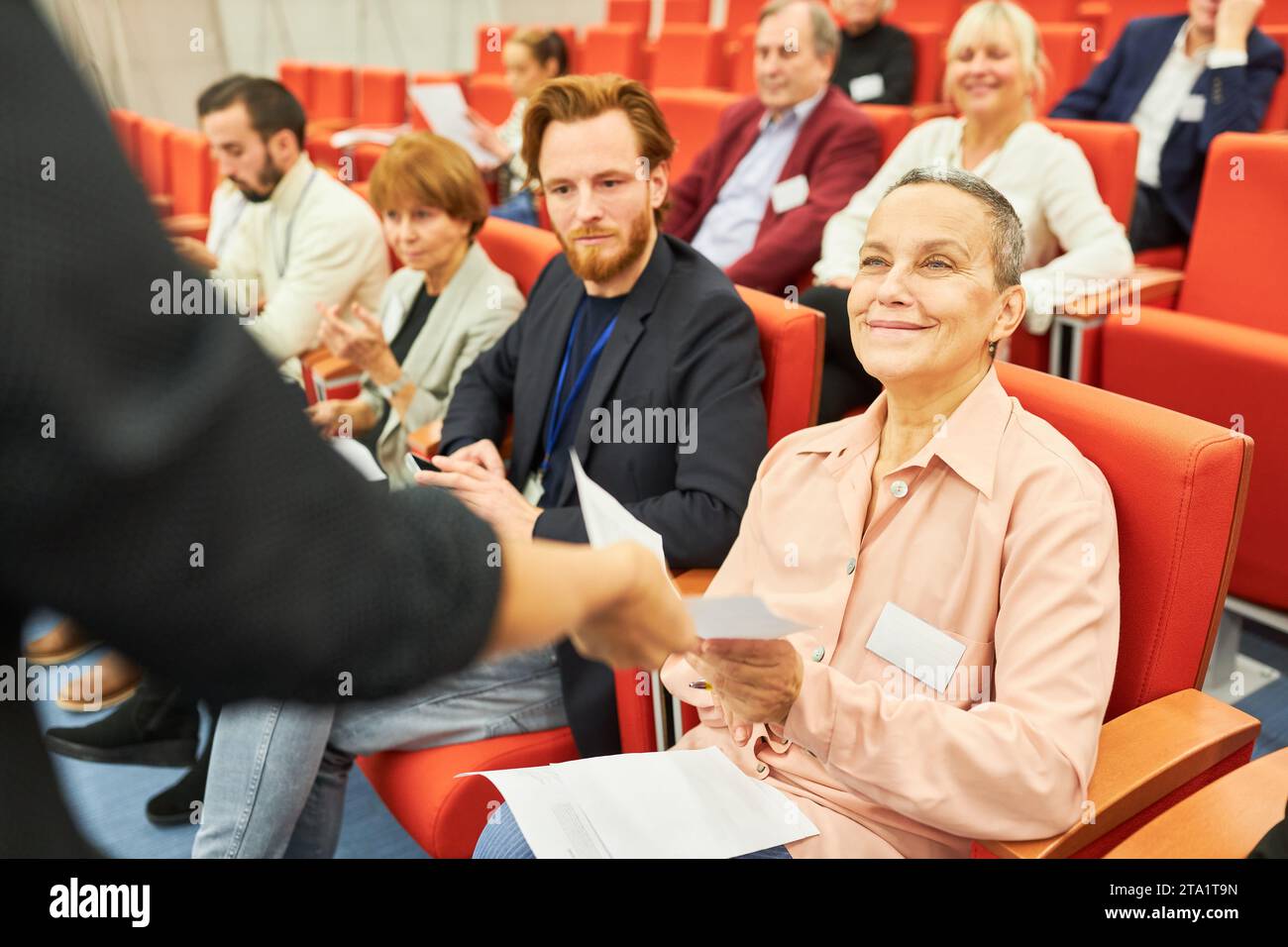 Smiling mature female professional receiving document during conference ...