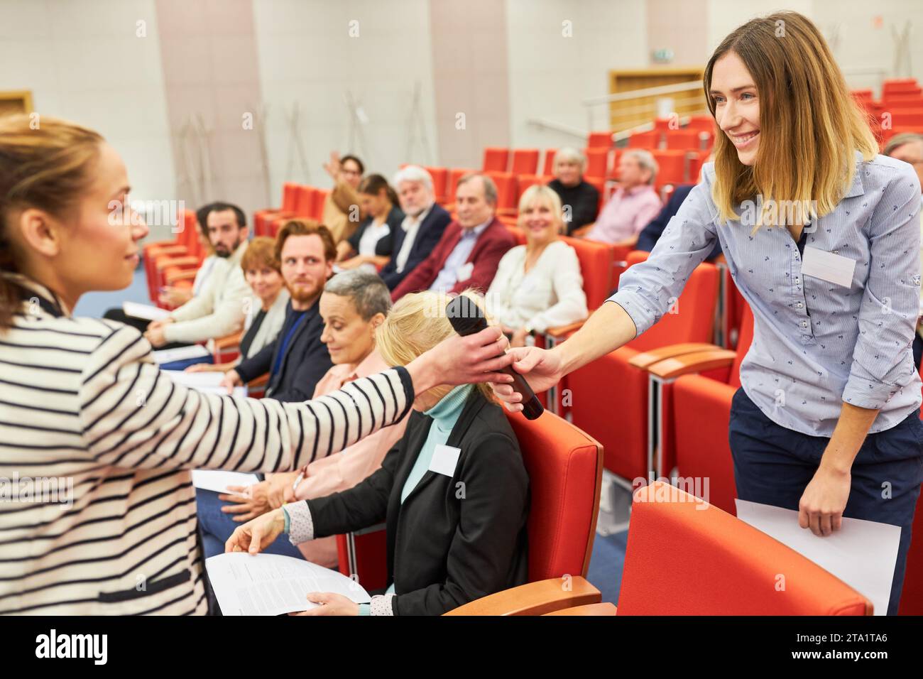 Female professional giving microphone to businesswoman during business ...