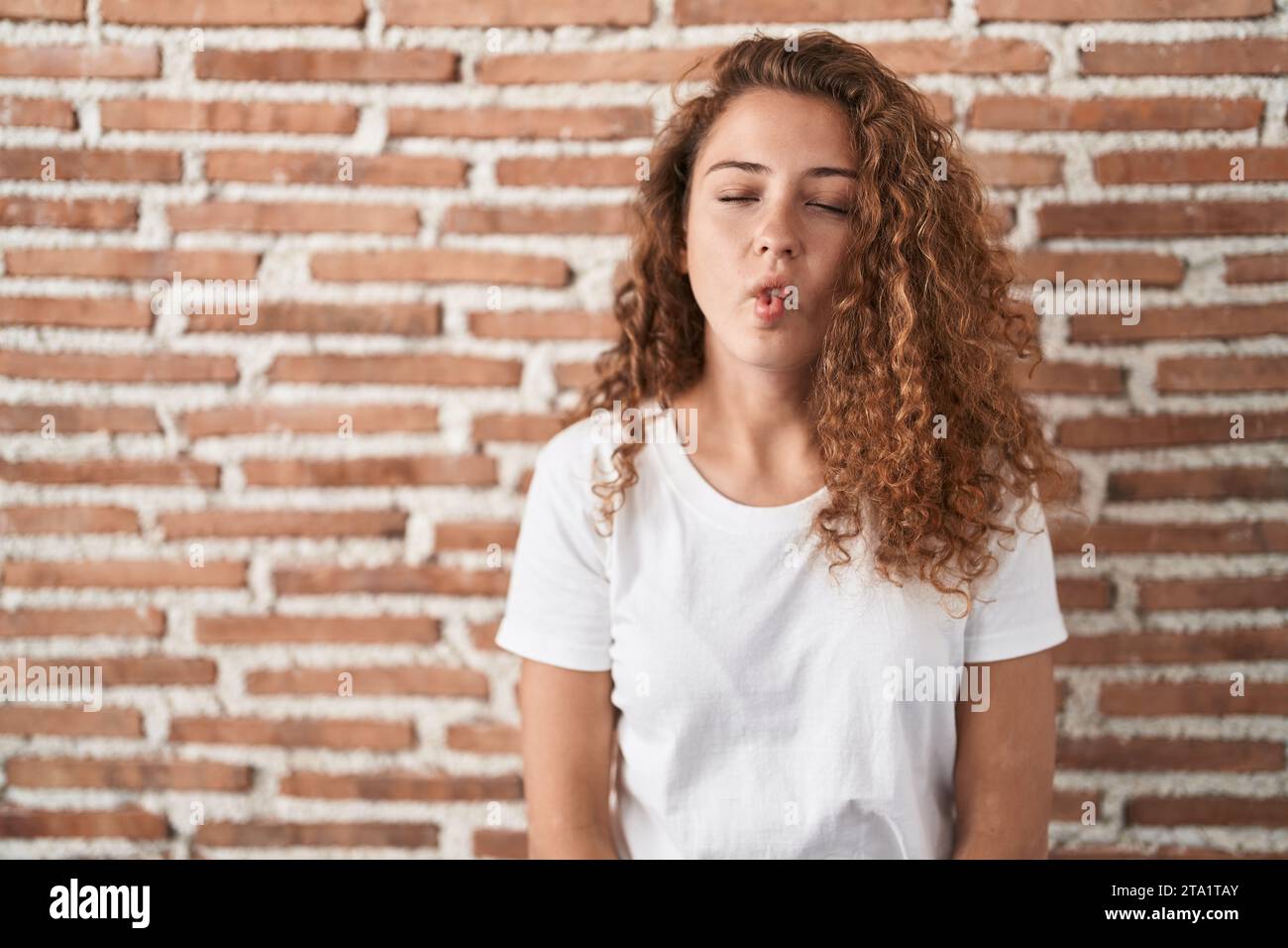 Young caucasian woman standing over bricks wall background making fish ...