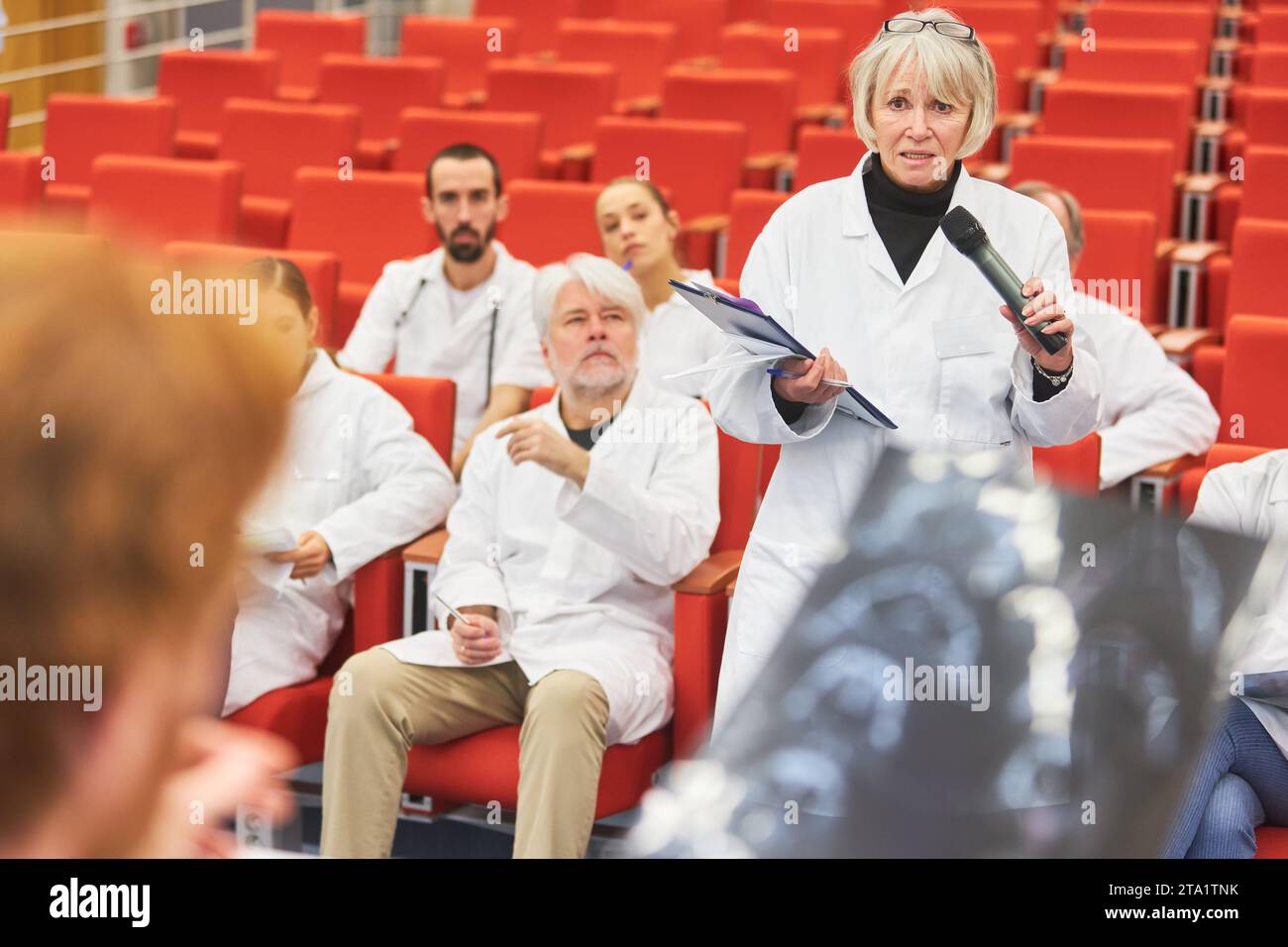 Female doctor in audience of medical conference asking question with ...