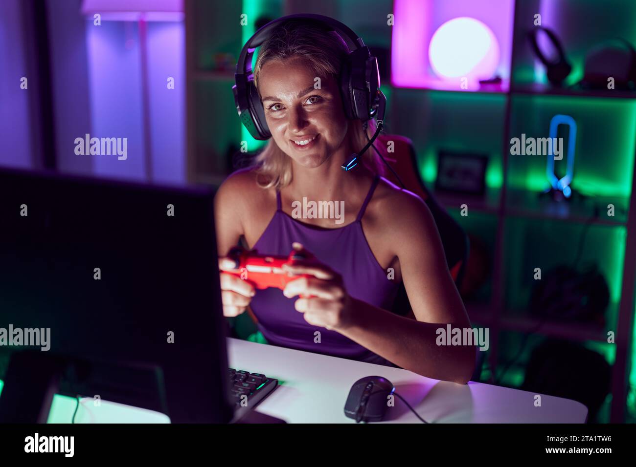 Young blonde woman streamer playing video game using joystick at gaming ...