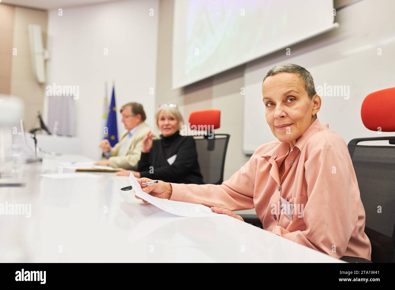 Portrait of female speaker reading document while sitting at panel in ...