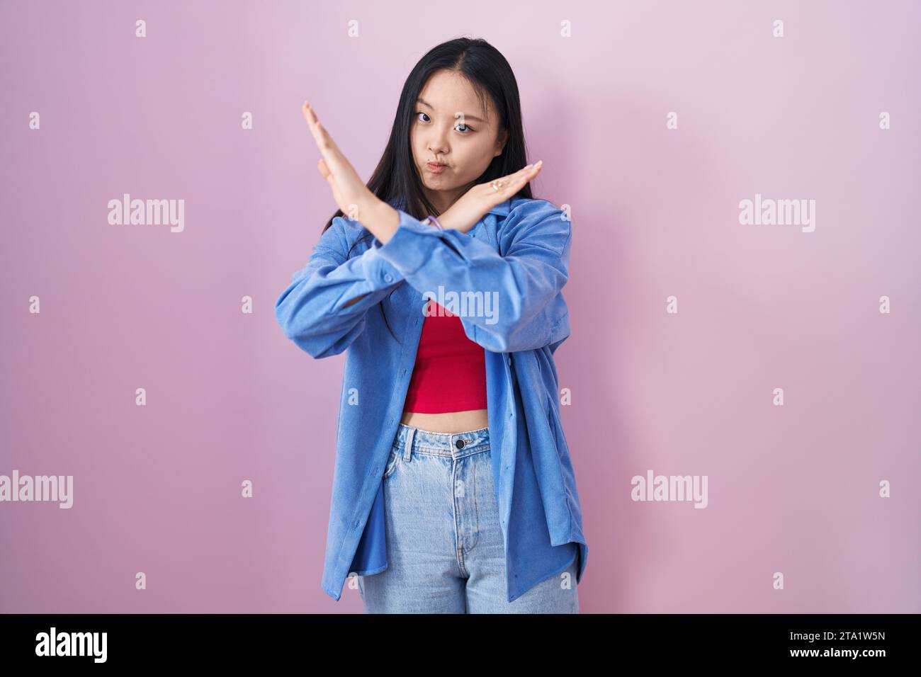 Young asian woman standing over pink background rejection expression ...