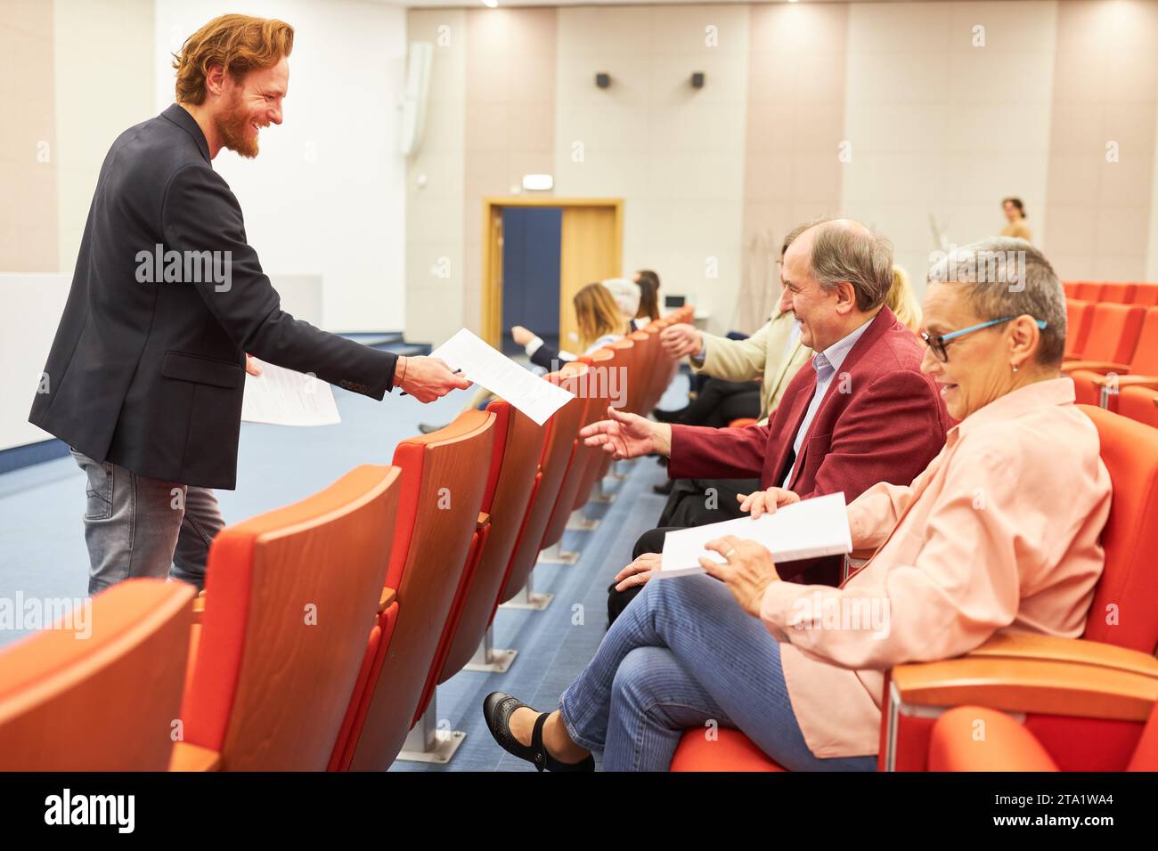 Smiling businessman giving form to professionals sitting in audience ...