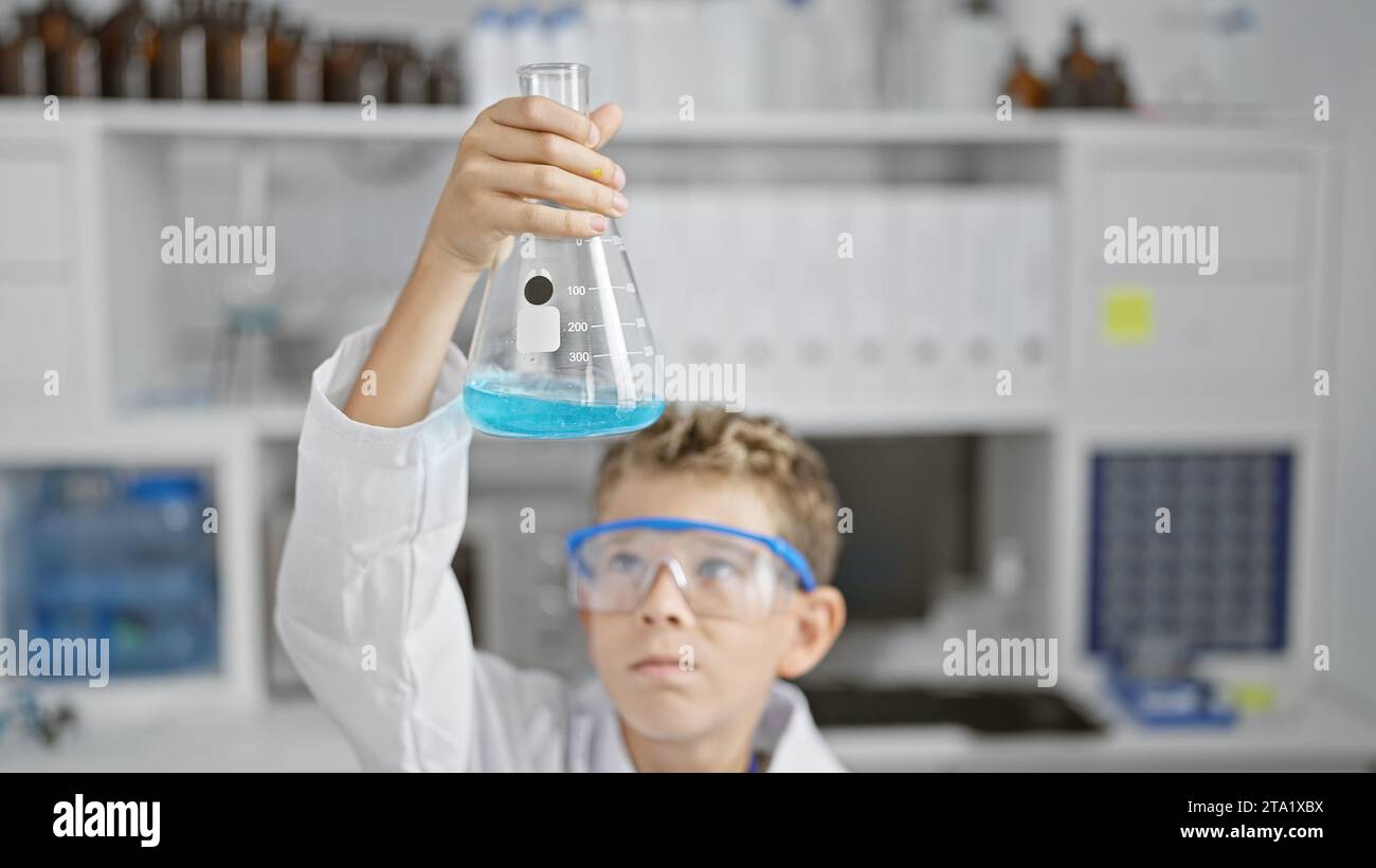 Adorable blond boy scientist totally immersed in experiment, looking at ...