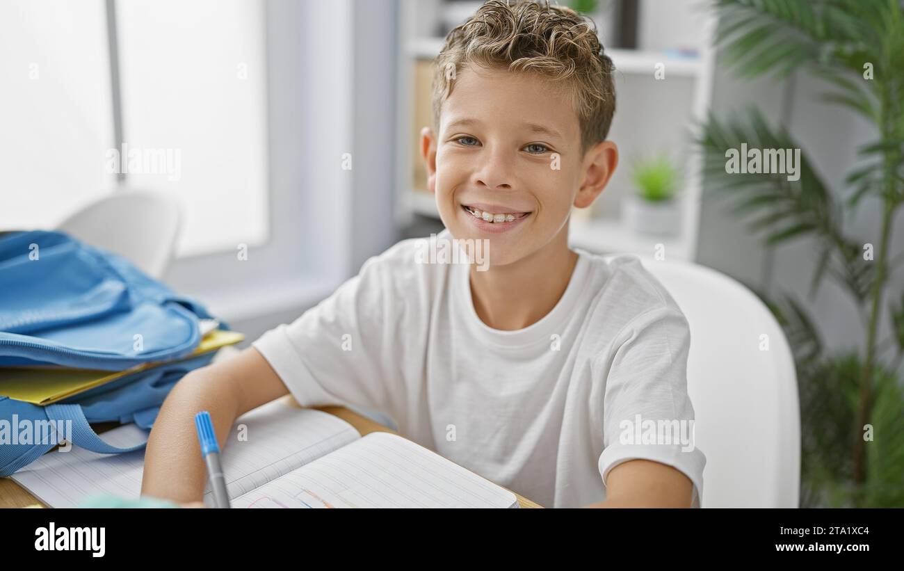 Cheerful blond boy student engrossed in taking notes at his desk ...