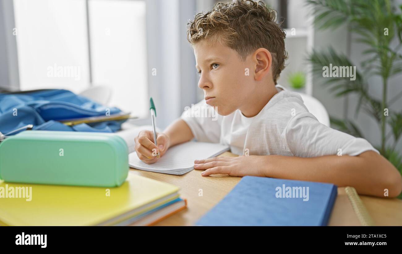 Adorable blond boy student, focused on learning, taking notes sitting ...